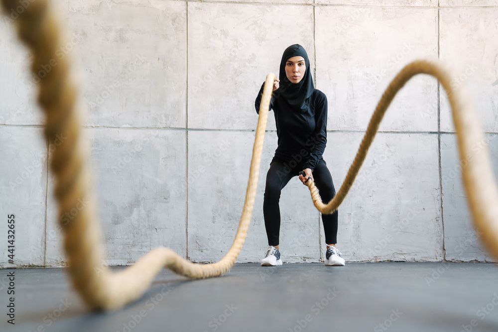 Young muslim woman in hijab working out with battle ropes indoors Stock ...