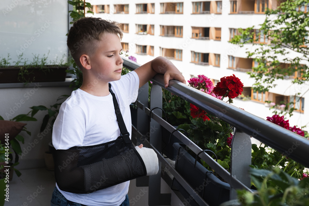 Sad child with a broken arm in a cast looks out into yard from the ...