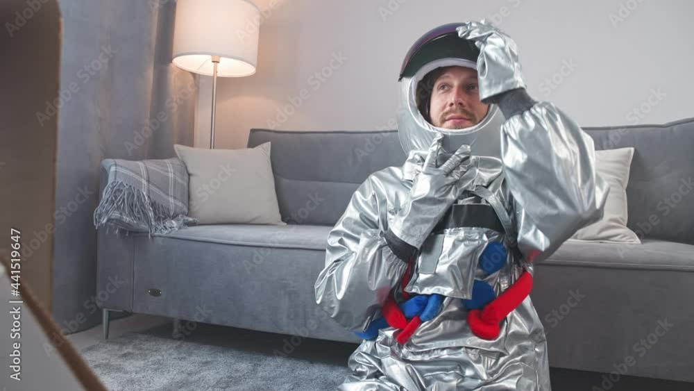 Man in an astronaut suit sits on the floor in living room next to a ...