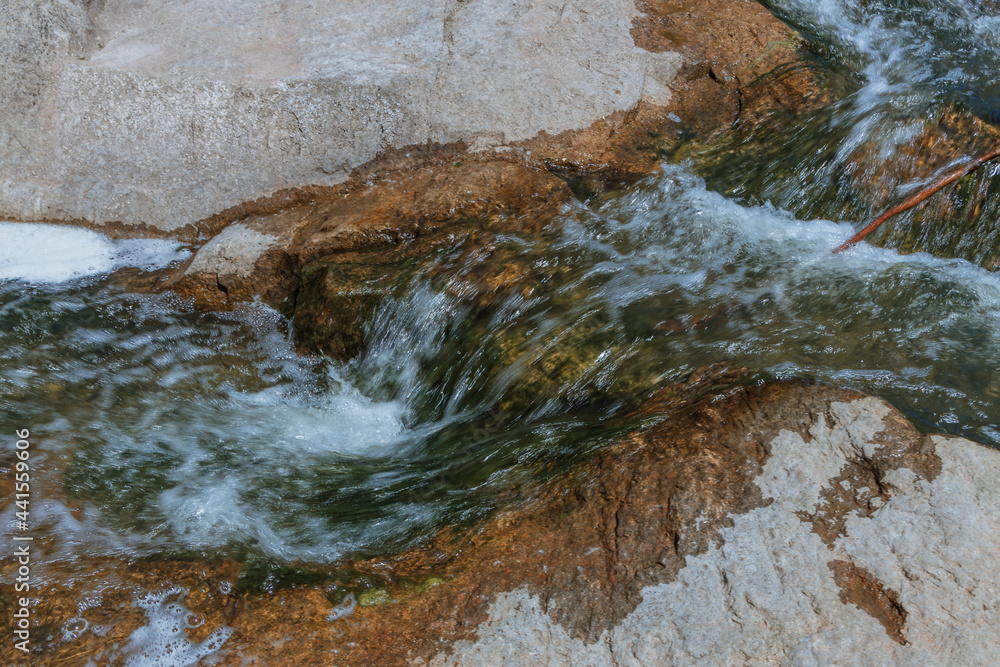 Selective focus close-up of clear stream water running over large rocks ...