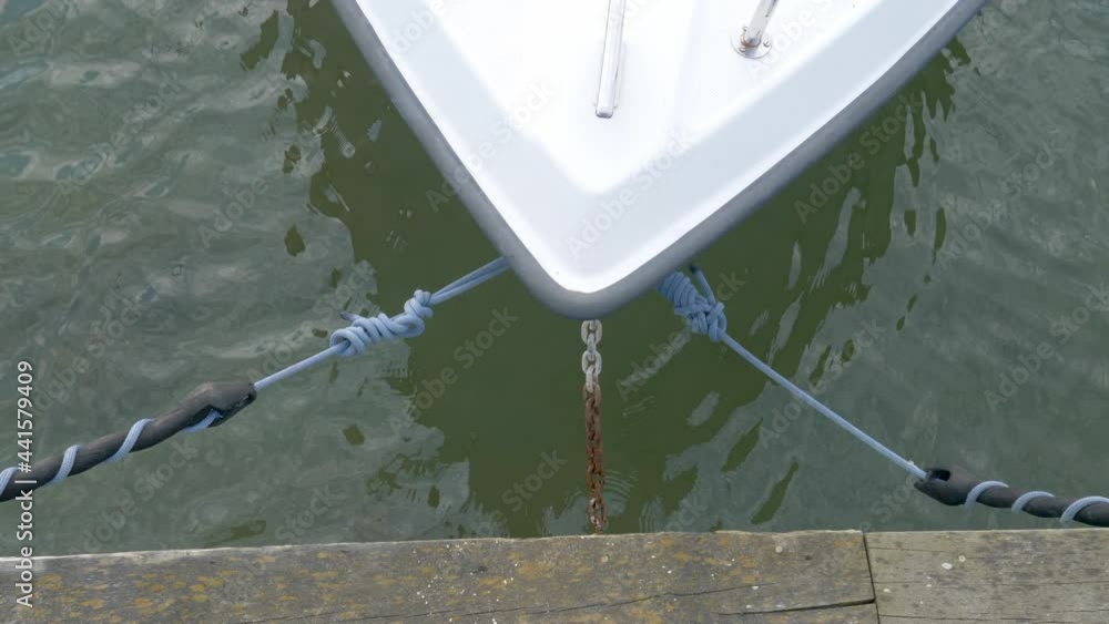 A boat is attached to a wooden pier. The boat is attached with two ...