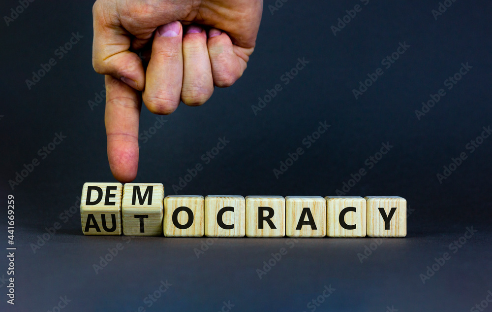 Democracy or autocracy symbol. Businessman turns wooden cubes and ... Democracy or autocracy symbol. Businessman turns wooden cubes and ...
