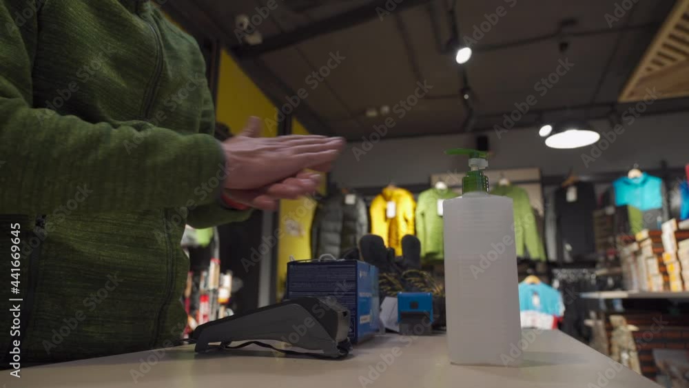 Salesperson at sports store uses hand sanitizer while serving customer ...