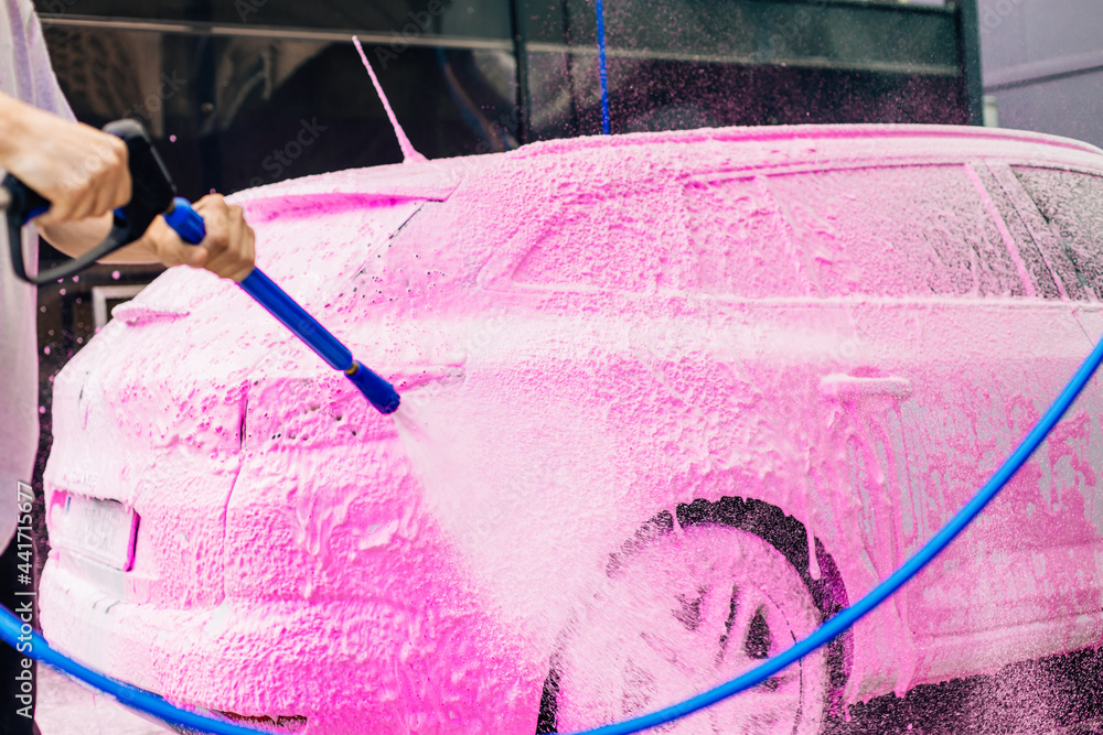 Car wash concept, Front view of white sports car covered with pink foam ...