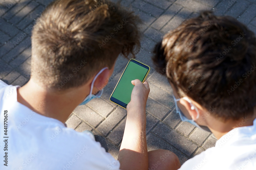 Two teenagers look at the screen of a smartphone. Two boys wearing ...