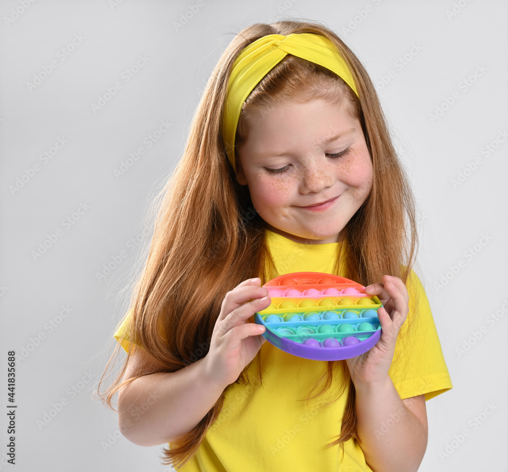 Cute little red-haired girl with colorful pop simple silicone toy with ...