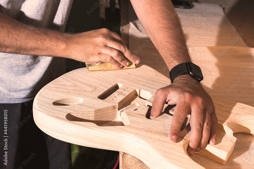 Close-up of the initial hand sanding process of a guitar body.Latin man ...