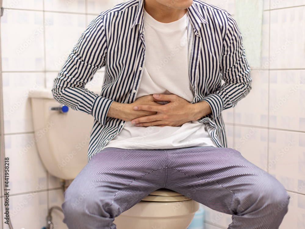 Young man holding his abdomen feels sick and constipation in the toilet ...