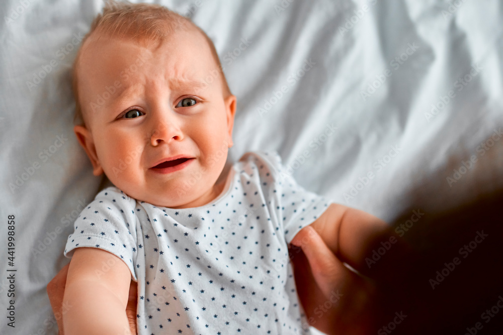 Cute nice little baby boy crying lying with her mom on bed at home. Sad ...