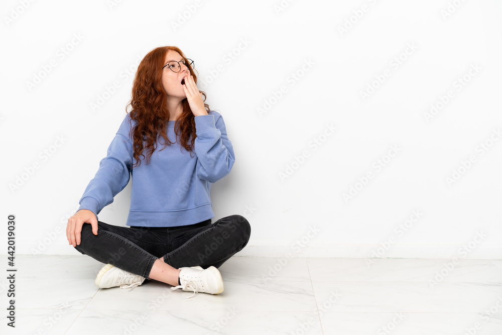 Teenager redhead girl sitting on the floor isolated on white background ...