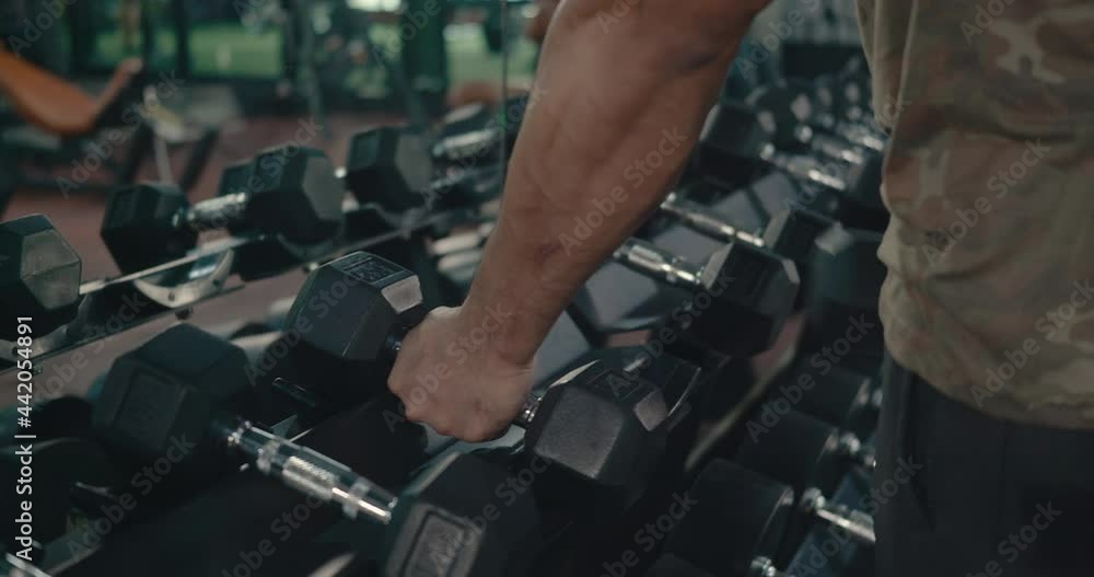 Close up man hands bodybuilder picking up or choosing dumbbell that are ...