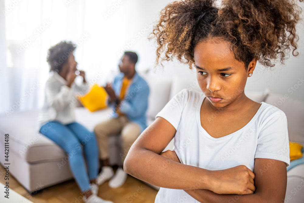 Sad little girl is looking at camera while her parents are arguing in ...