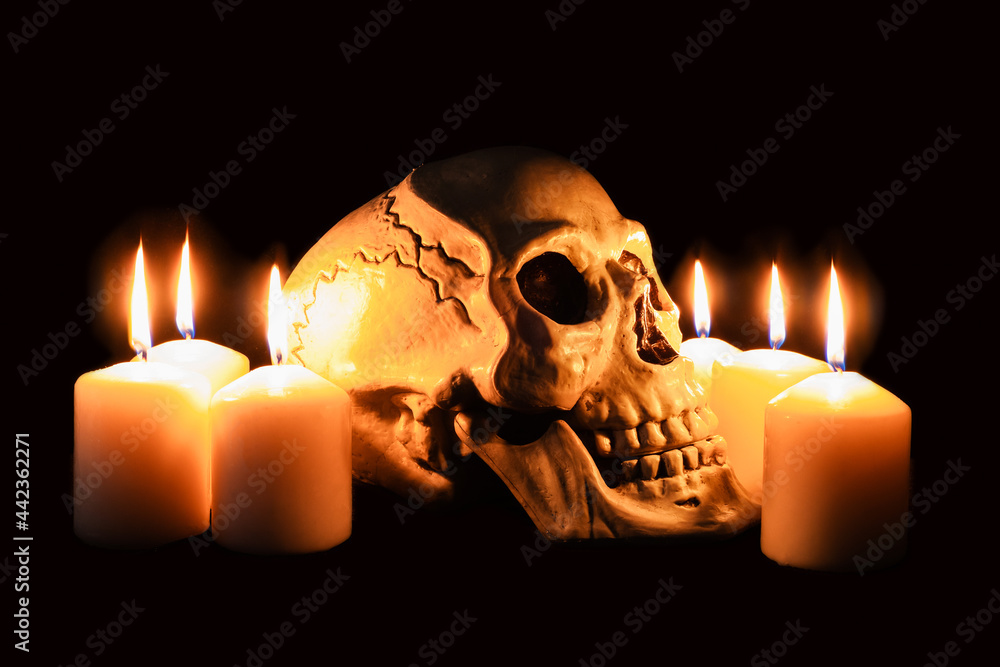 Human skull in profile among burning candles in the dark, scary still ...