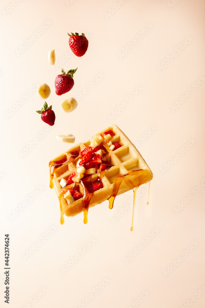 flying waffle with maple, bananas and strawberries. brown background ...