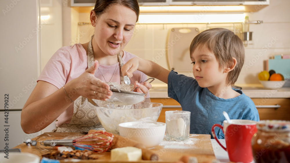 Little boy pouring flour in sieve for sifting it and making dough ...