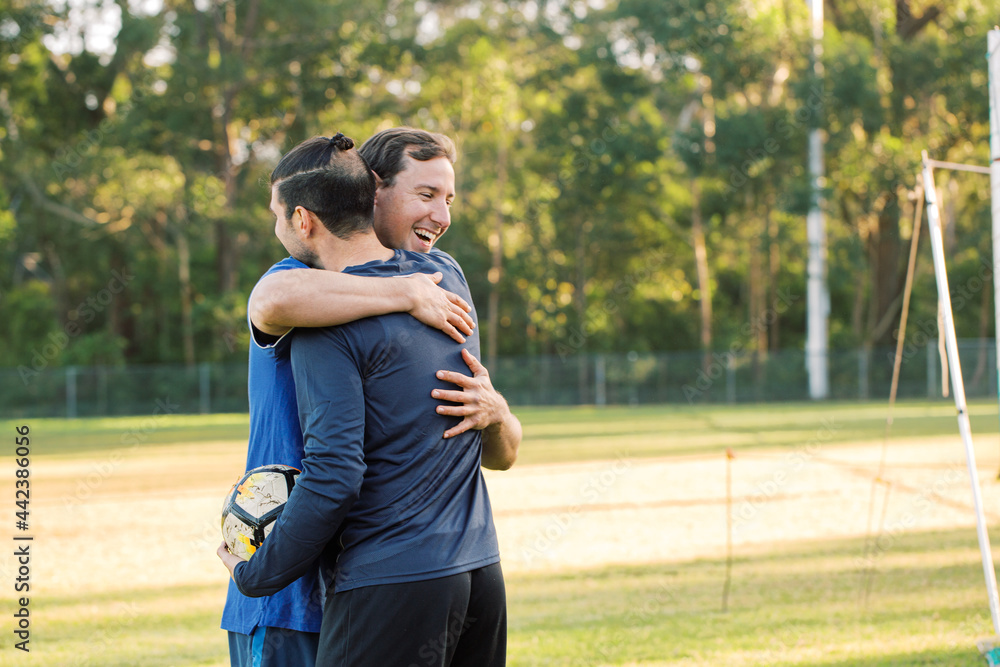 Two smiling young men on the soccer field with a soccer ball hugging ...