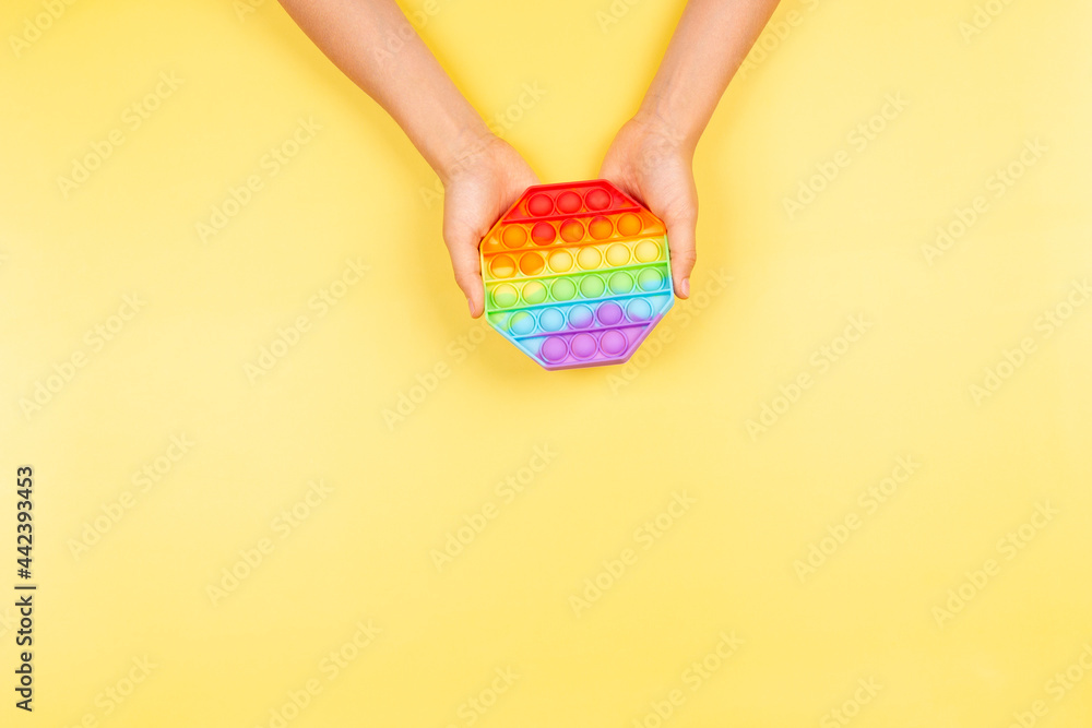 Kid hand holding pop it fidget toy on yellow background. Push pop-it ...