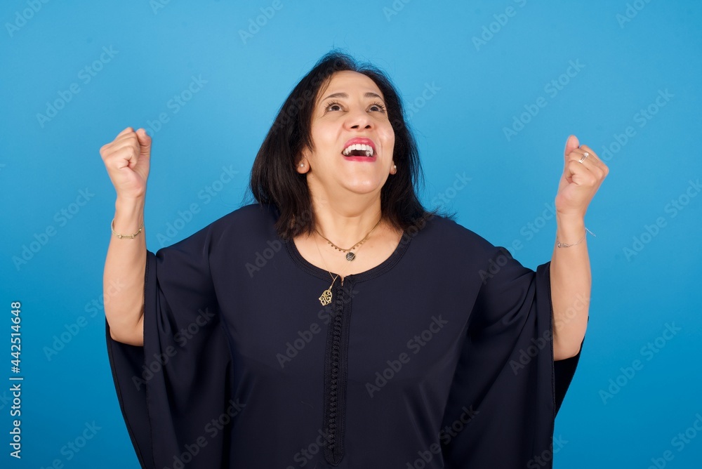 middle aged Arab woman standing against blue background looks with ...