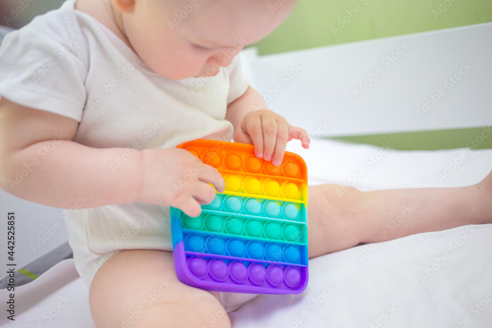 Little baby girl sitting at home on the bed, playing Pop-it new anti ...