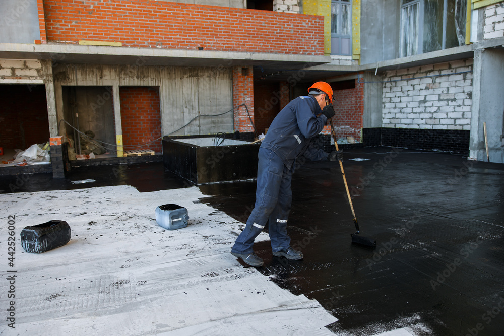 Waterproofing coating. A worker applies bitumen mastic to the ...