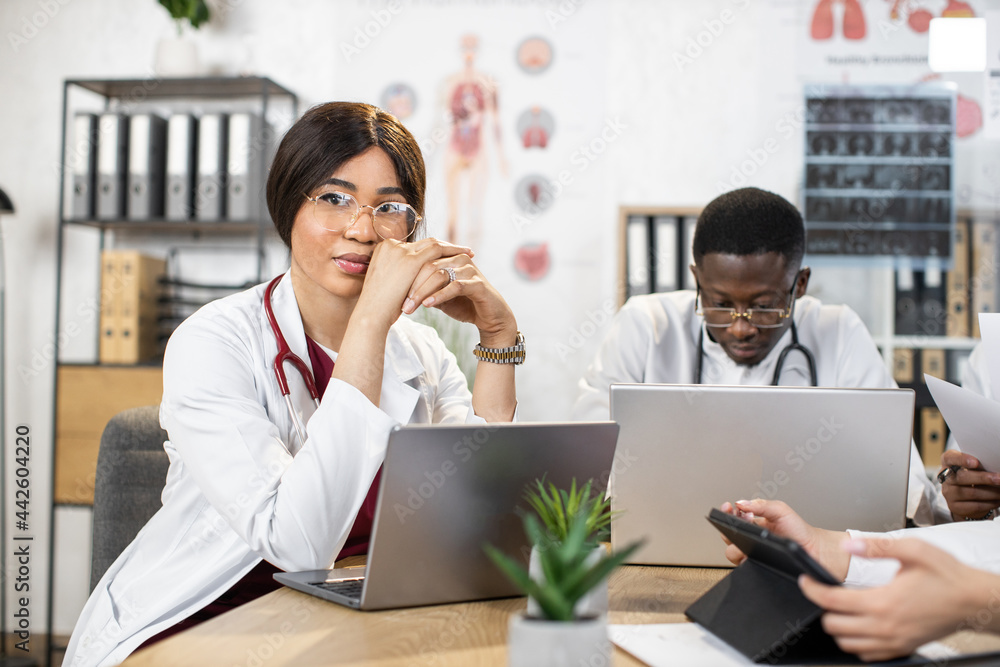 Multiracial colleagues in medical white coats working on laptops and ...