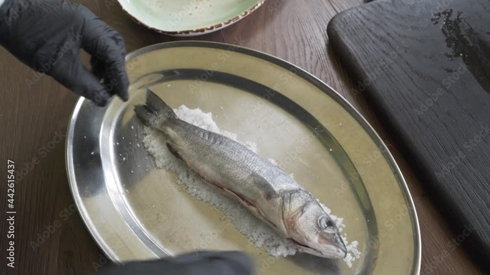 Sea bass covered with salt . The cook cleans the baked fish from salt ...