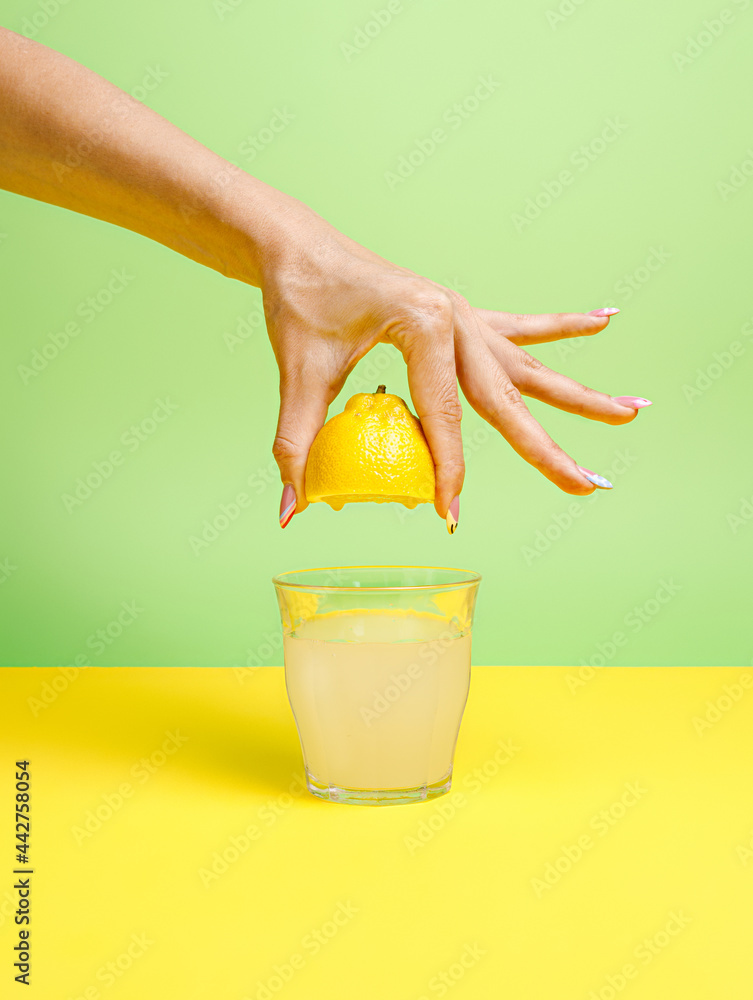 A woman's hand squeezing half of a lemon and making a glass of icy cold ...