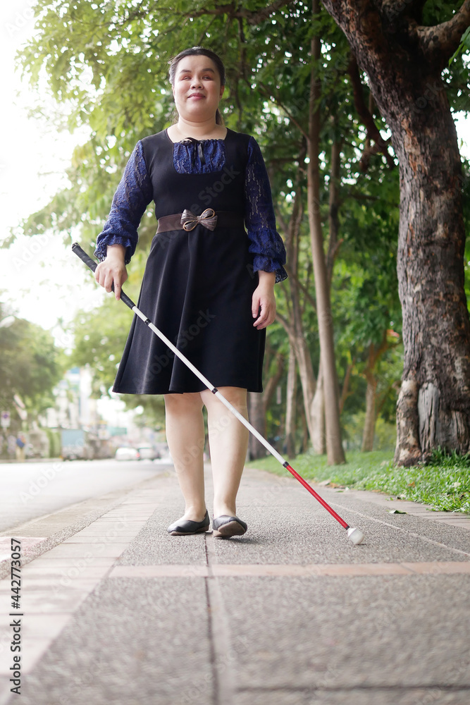 Asian blind person woman walking on sidewalk with a long white cane a ...