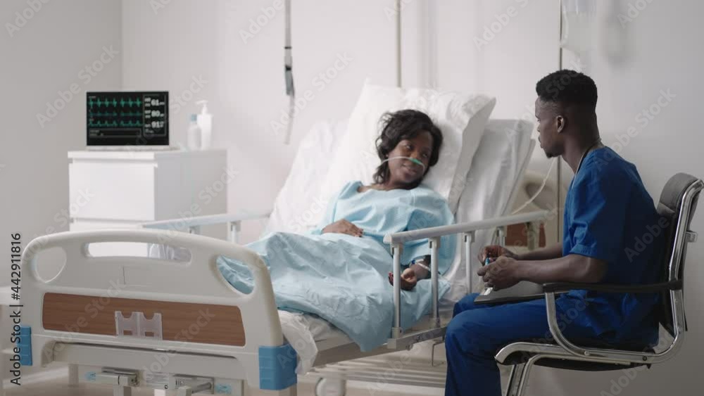 A black male doctor is talking to a black female patient lying on a ...