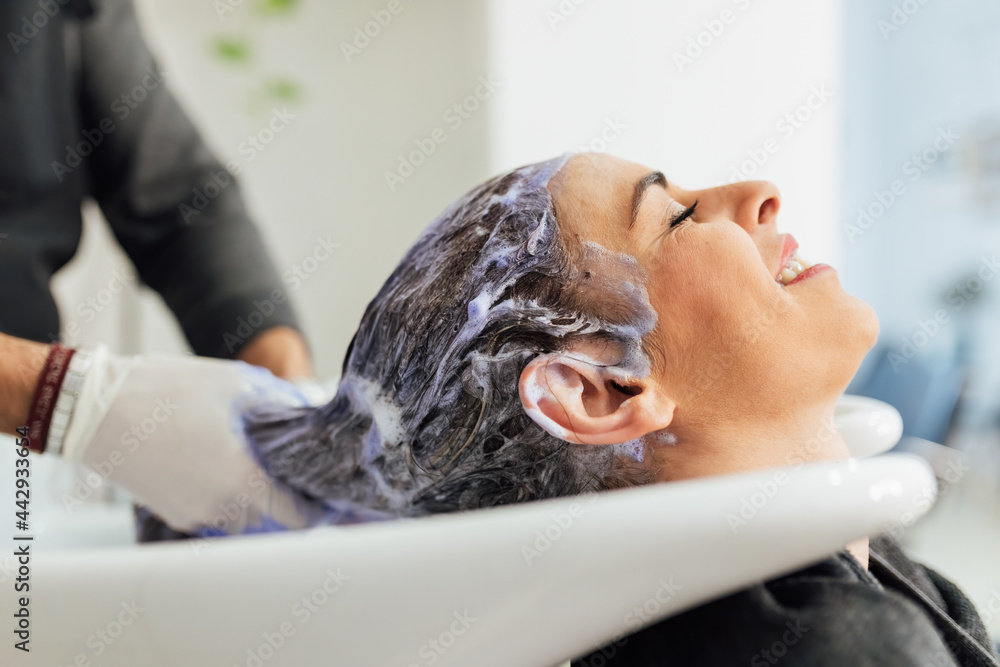 Professional hairstylist washing hair of female customer with shampoo ...