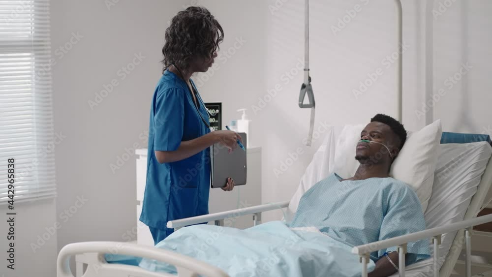 A black female doctor is talking to a black male patient lying on a ...
