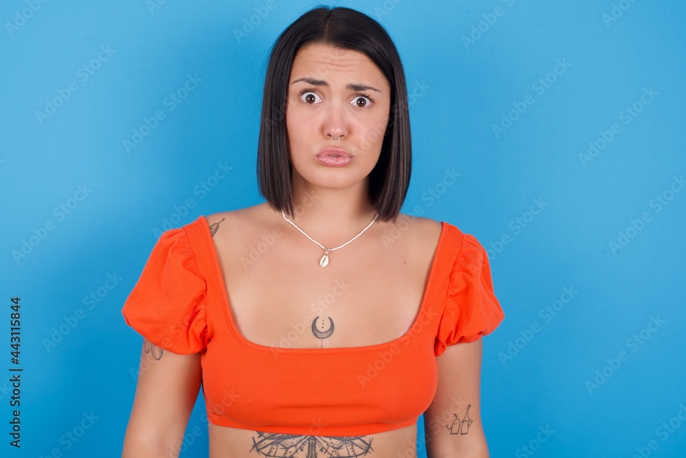 young beautiful tattooed girl wearing orange top standing against blue ...