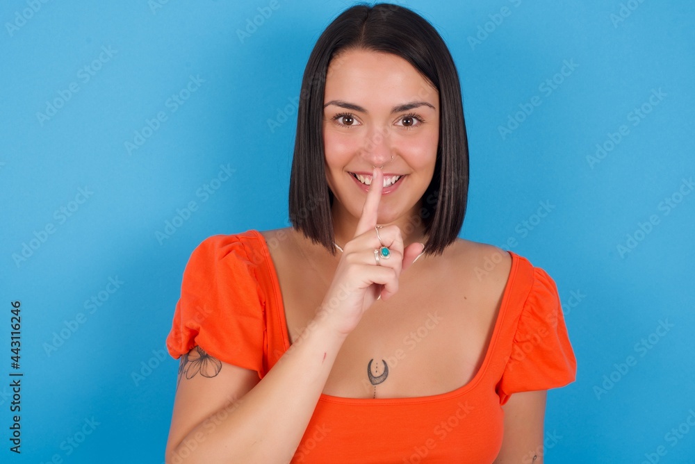 Smiling young beautiful tattooed girl wearing orange crop top standing ...
