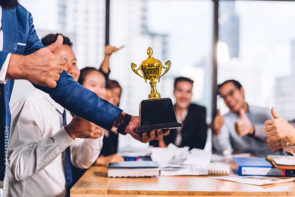 Successful group of casual business relaxing and holding gold trophy ...