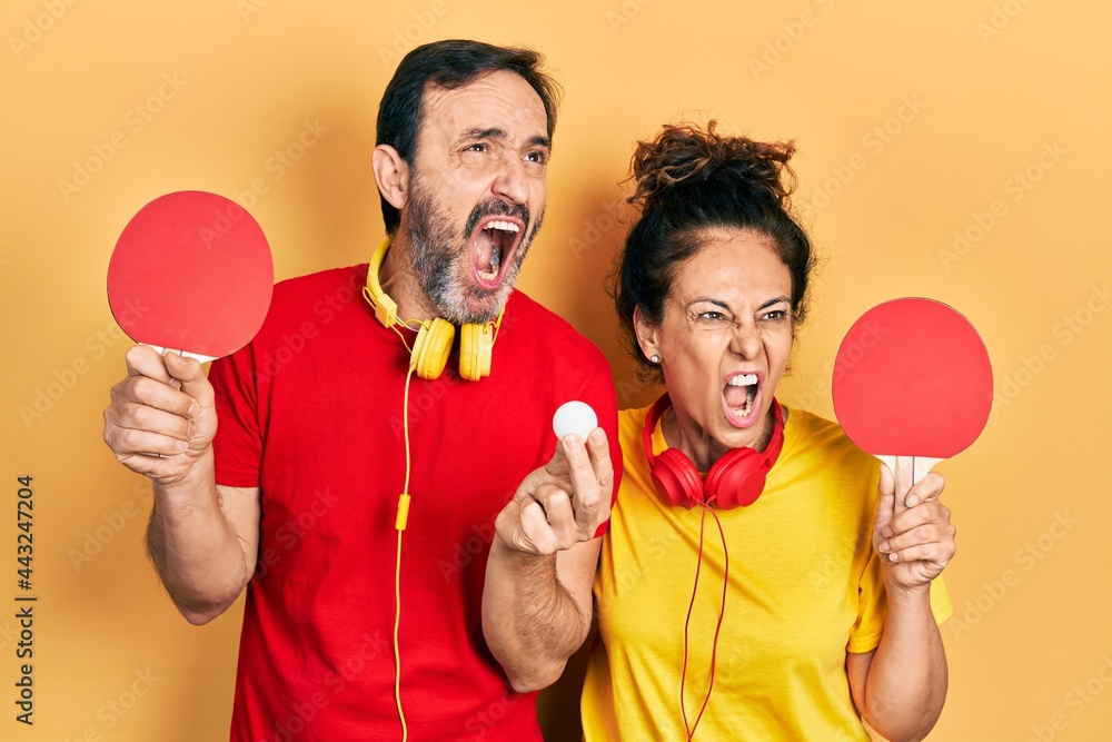 Middle age couple of hispanic woman and man holding red ping pong ...