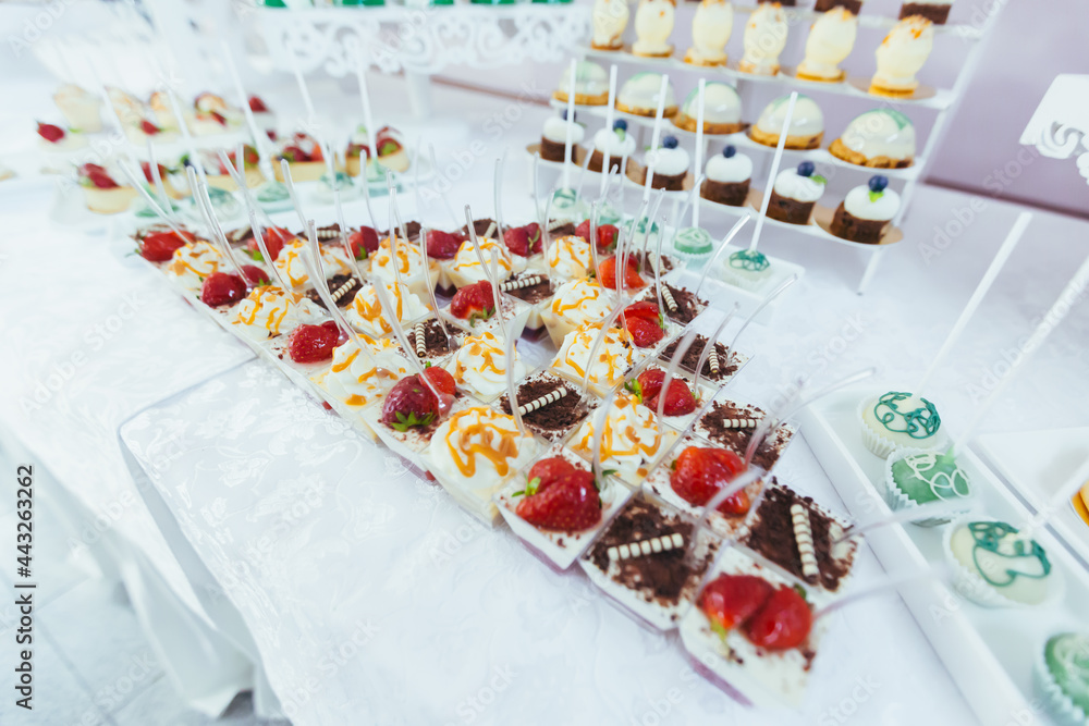 Candy bar. White festive table with deserts, strawberry tartlet and ...