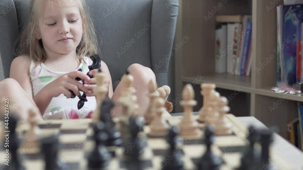 A cute little girl learns to play chess at home. The mischievous little ...