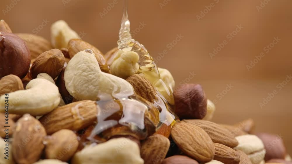 Trickle of golden honey flows down a pile of nuts in slow motion. Honey ...