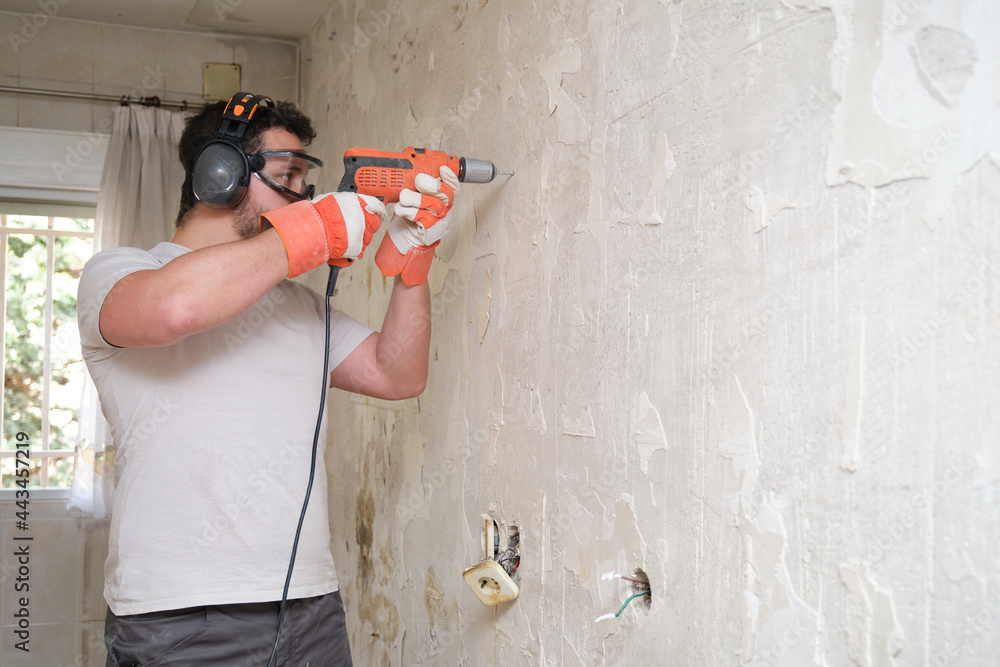 Builder drilling holes in a wall with an electric drill at the ...