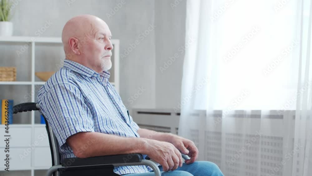 Disabled old man is sitting in a wheelchair at home alone. A ...