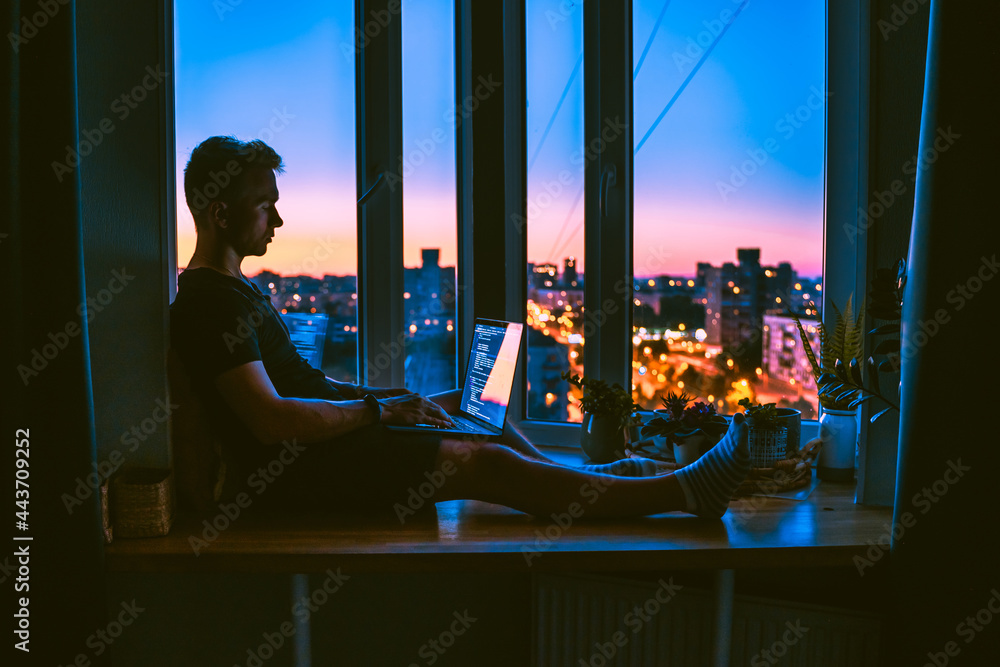 A young programmer is coding on a laptop in the dark sitting on a ...