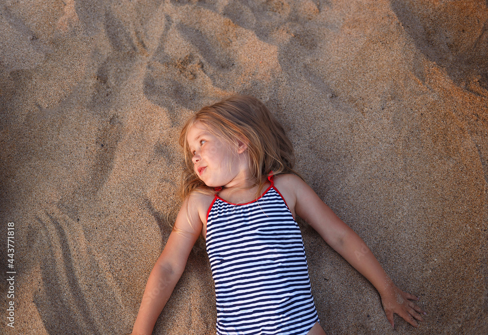 little cute girl in a striped swimsuit lies on a sandy beach Stock ...