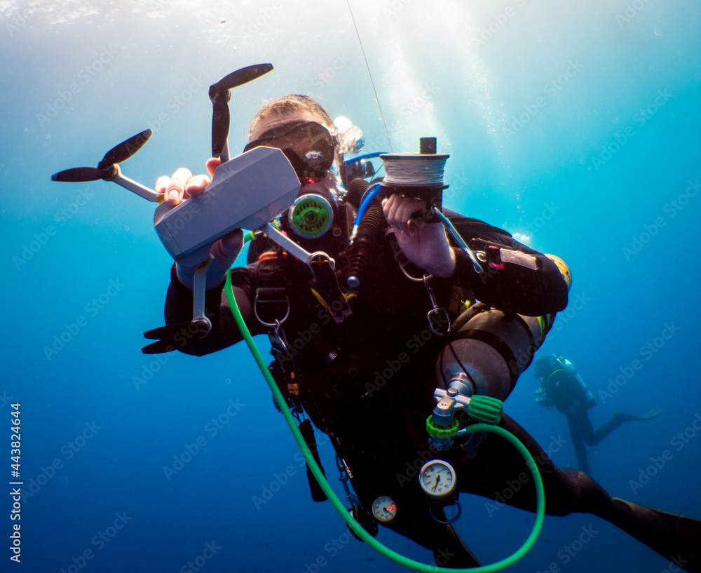 Women diver with drone underwater shooting on a blue background. Diver ...