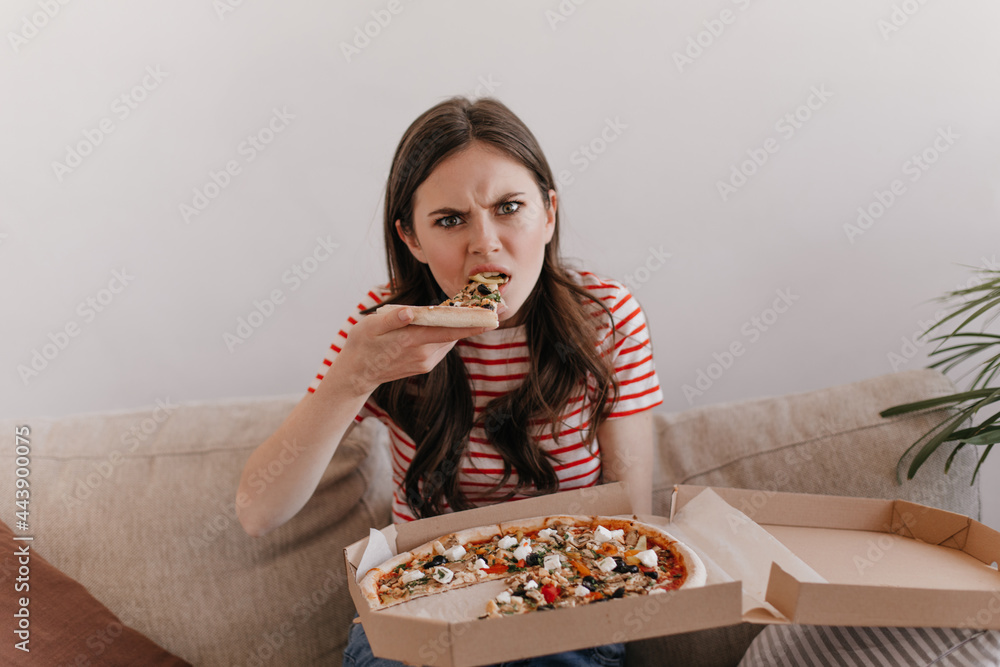 Girl in jeans and striped shirt with hungry look bites fresh pizza ...
