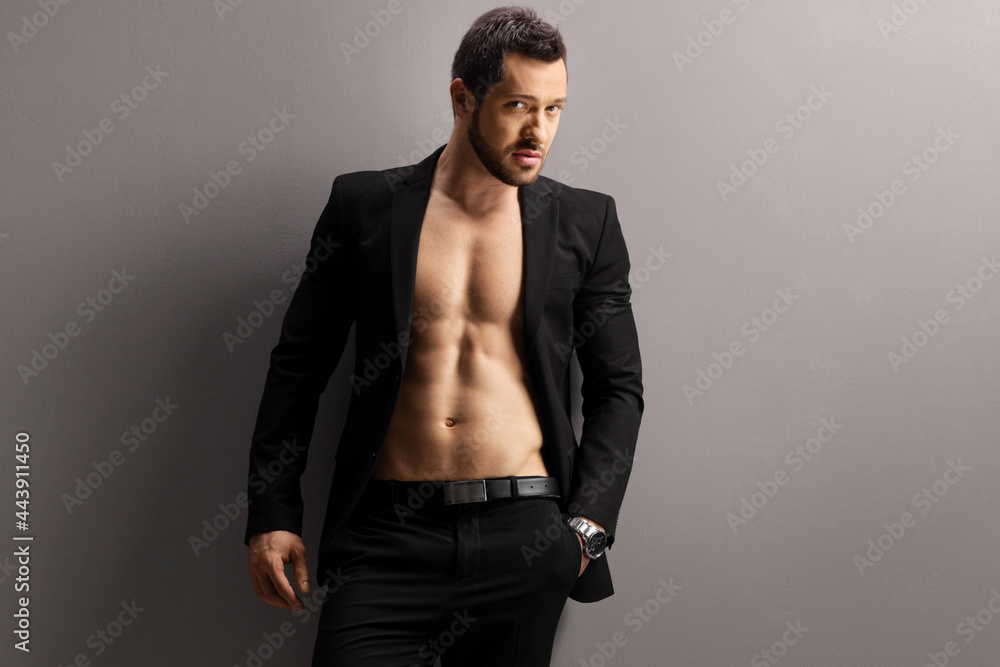 Male model in a black suit posing shirtless and looking at the camera ...