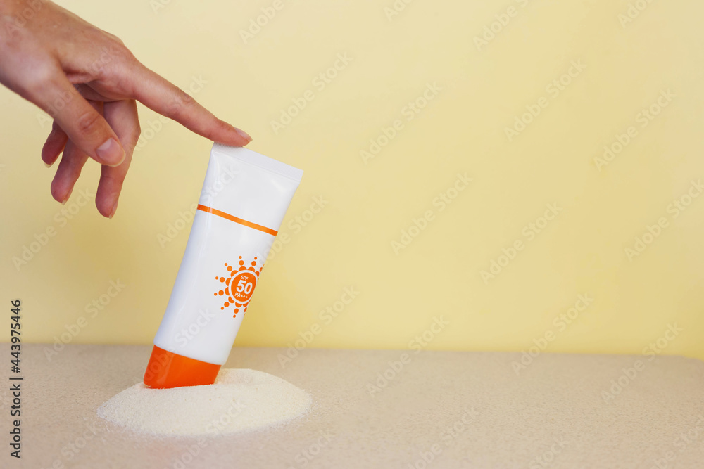 female hand touches a tube of sunscreen on a beige background with sand ...