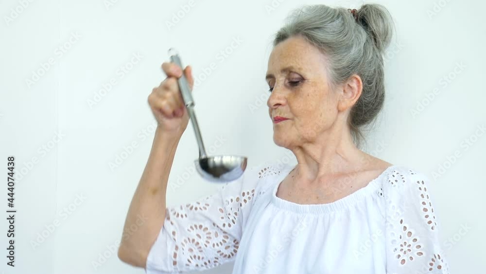 Emotional senior woman with silver hair is holding metal ladle or scoop ...