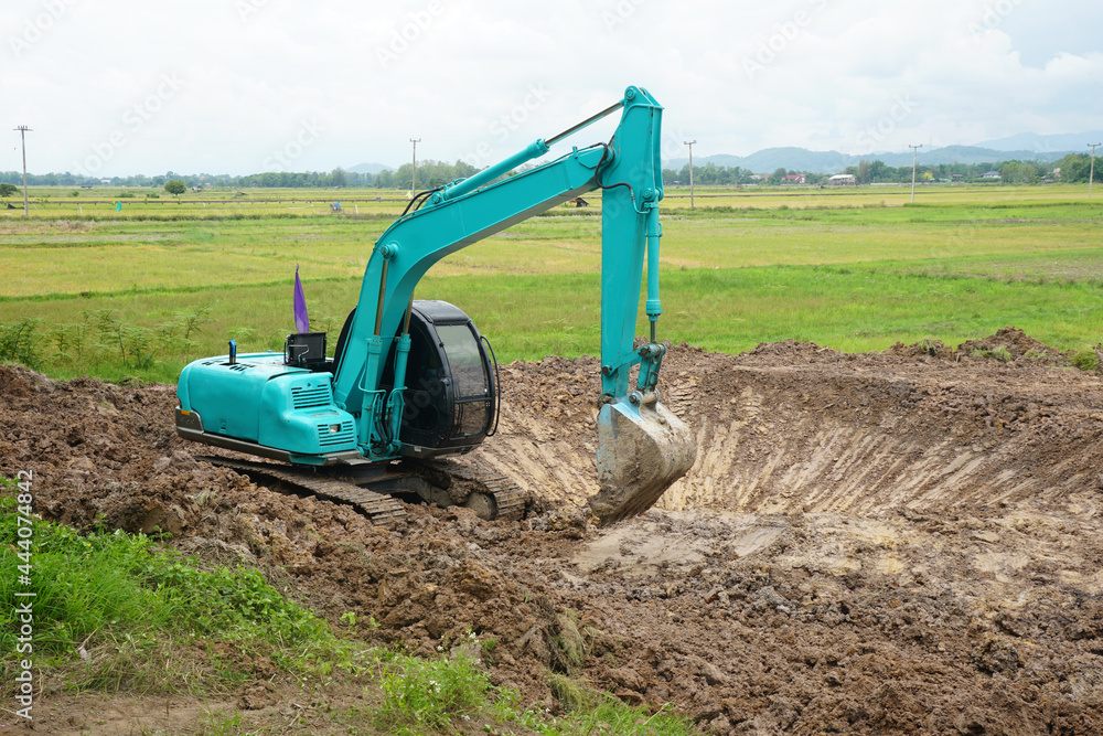 A blue excavator is digging a swamp in the middle of a field for ...