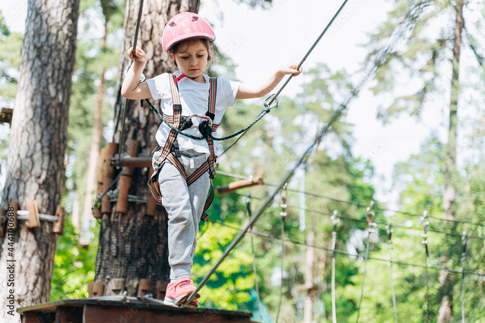 Little girl walks on a rope, hands holding a rope. A child in a rope ...