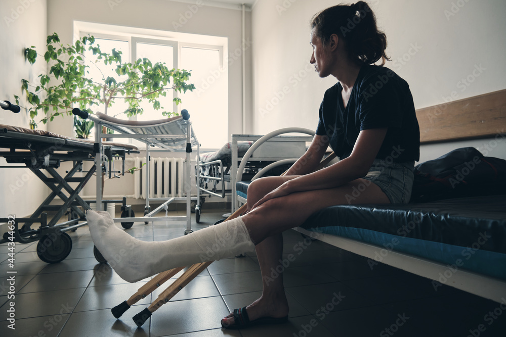 A woman with a broken leg sits on a hospital couch and looks out the ...
